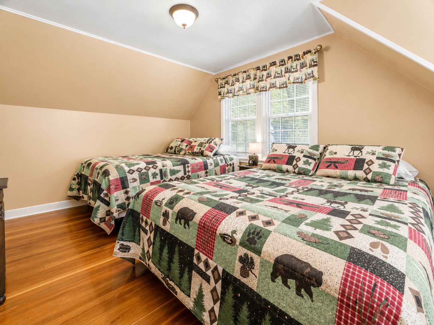 Quarto com duas camas, janela com persianas, luminária no teto e piso de madeira.