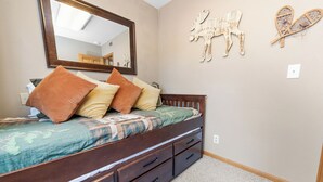 Quarto com cama de madeira, várias almofadas, espelho e detalhes decorativos na parede.