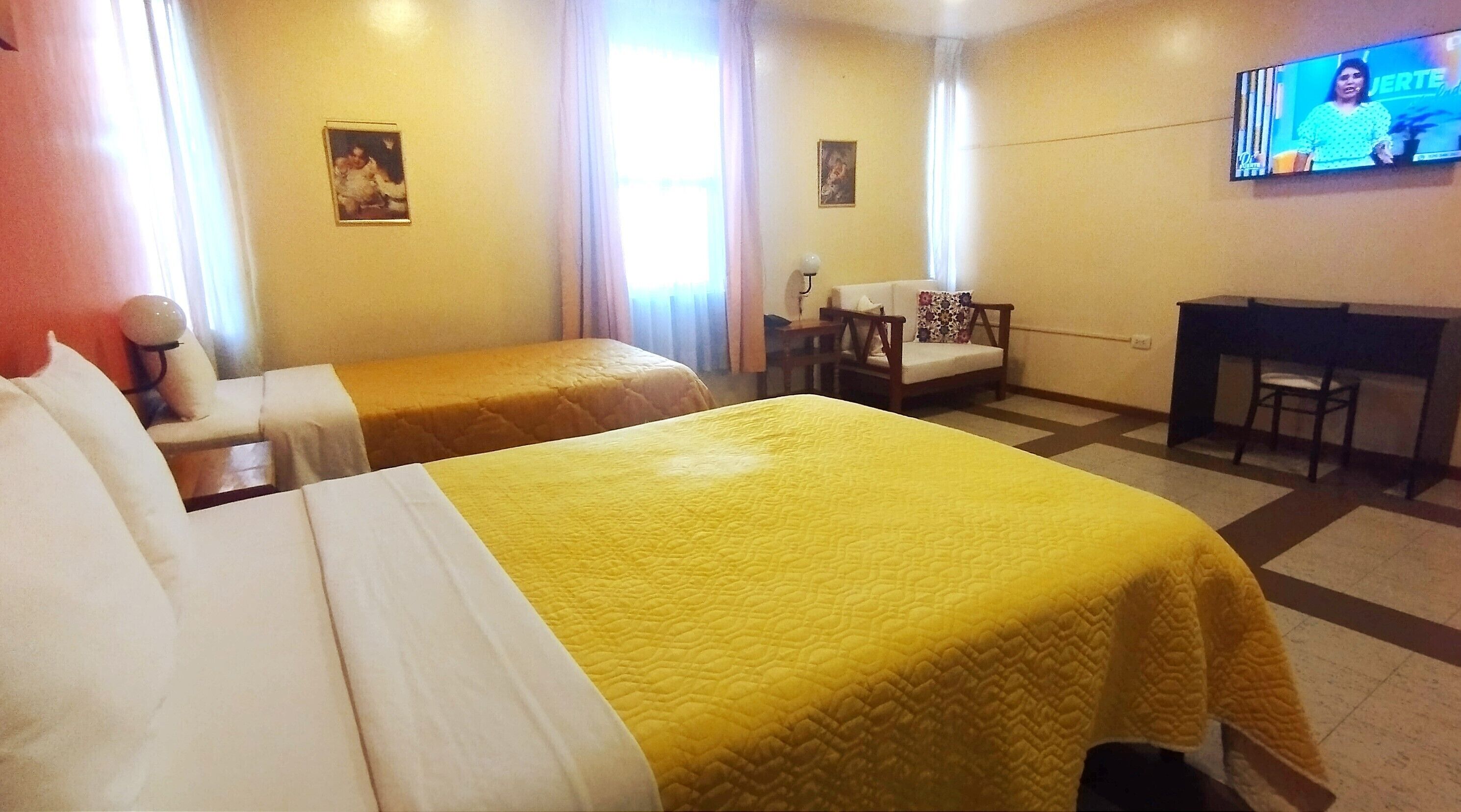 Quarto de hotel com duas camas, uma escrivaninha, uma cadeira e uma televisão na parede.