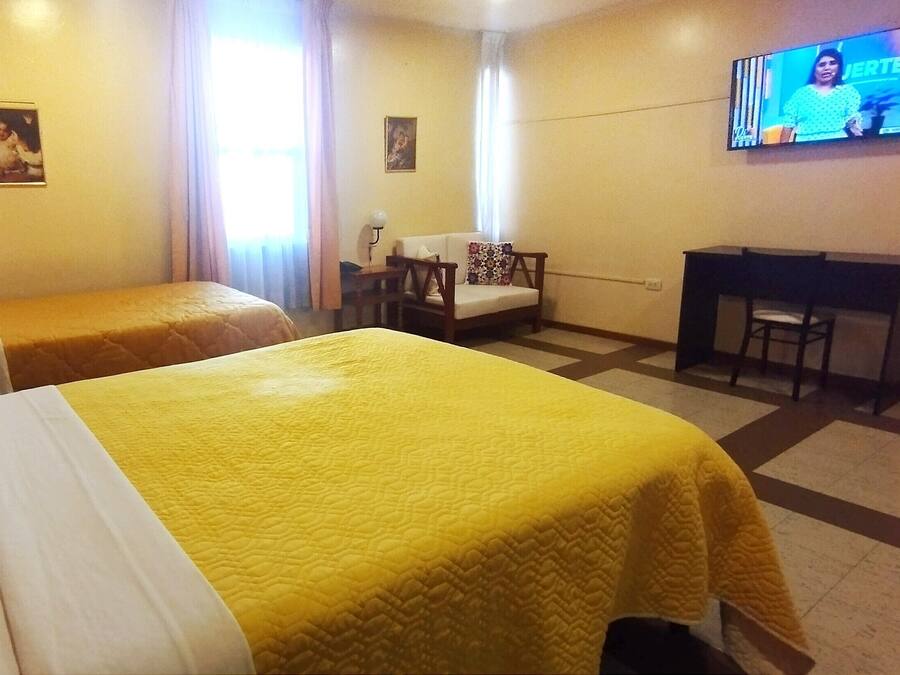 Quarto de hotel com duas camas, uma escrivaninha, uma cadeira e uma televisão na parede.