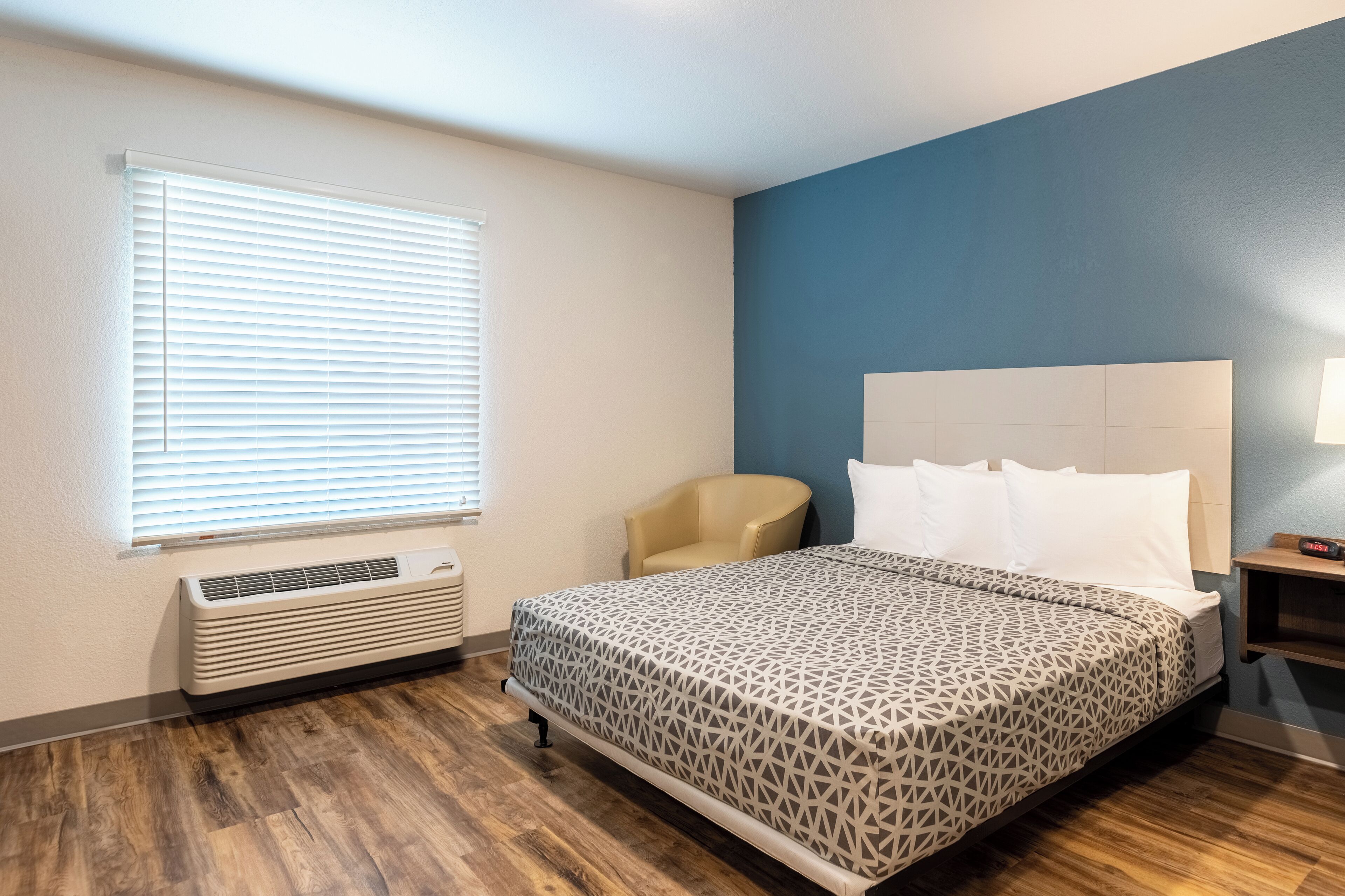 Quarto com cama, cadeira, mesa de cabeceira, aquecedor e janela com persianas.