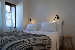 Quarto com cama, mesa de cabeceira e janela com cortinas.