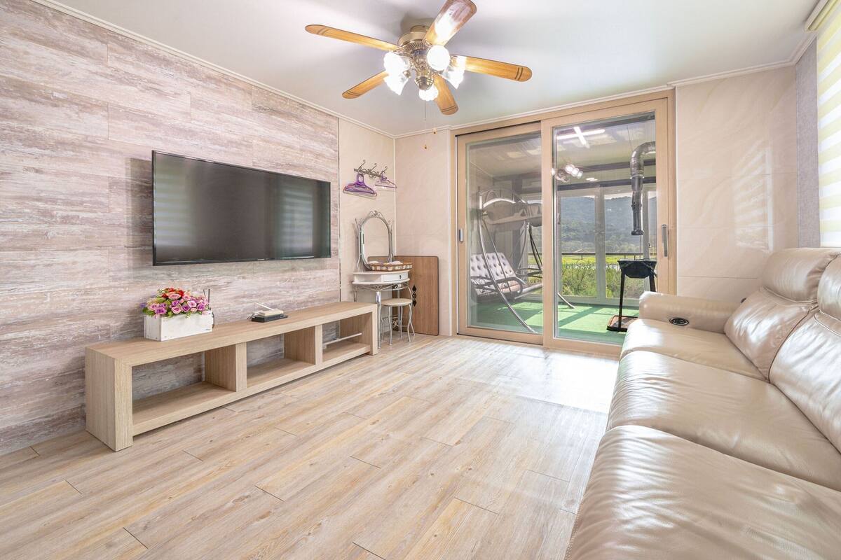 Uma sala de estar moderna com televisão de tela plana, painel de entretenimento de madeira, sofá de couro e ventilador de teto.