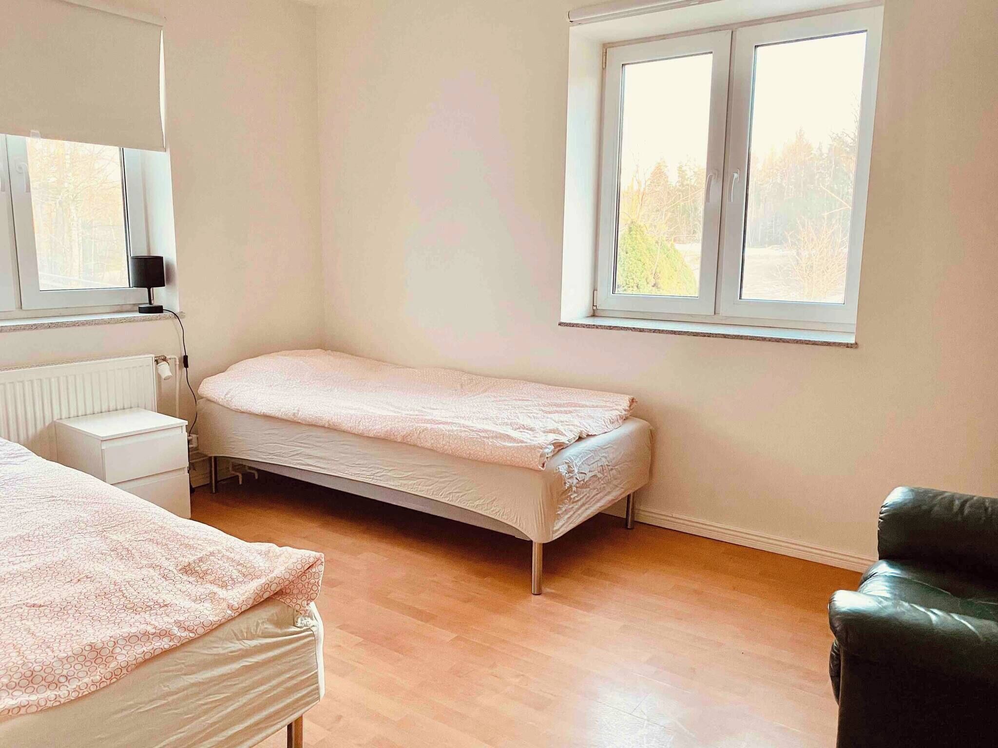 Um quarto pequeno e modesto, com uma cama de solteiro, uma cadeira e uma janela.