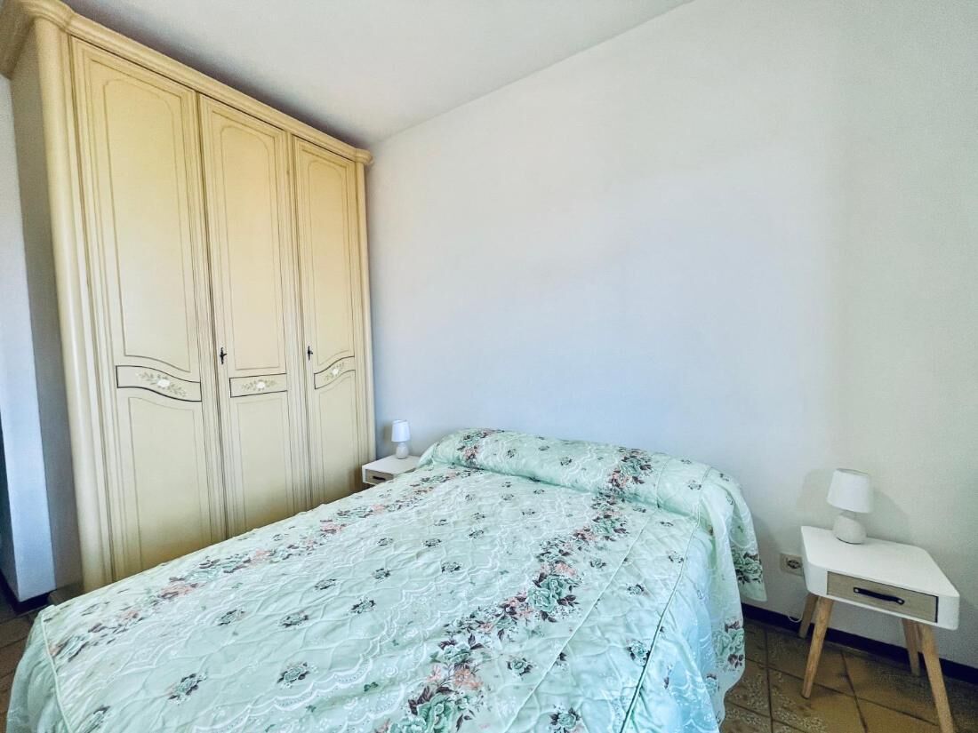 Um quarto com cama, guarda-roupa, mesa de cabeceira e criado-mudo.