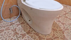 Sanitário com a tampa fechada, num banheiro com ladrilhos estampados no chão e azulejos laranja nas paredes.