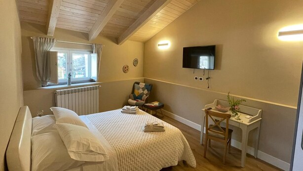 Quarto com cama, escrivaninha, cadeira, televisão e janela com cortinas.