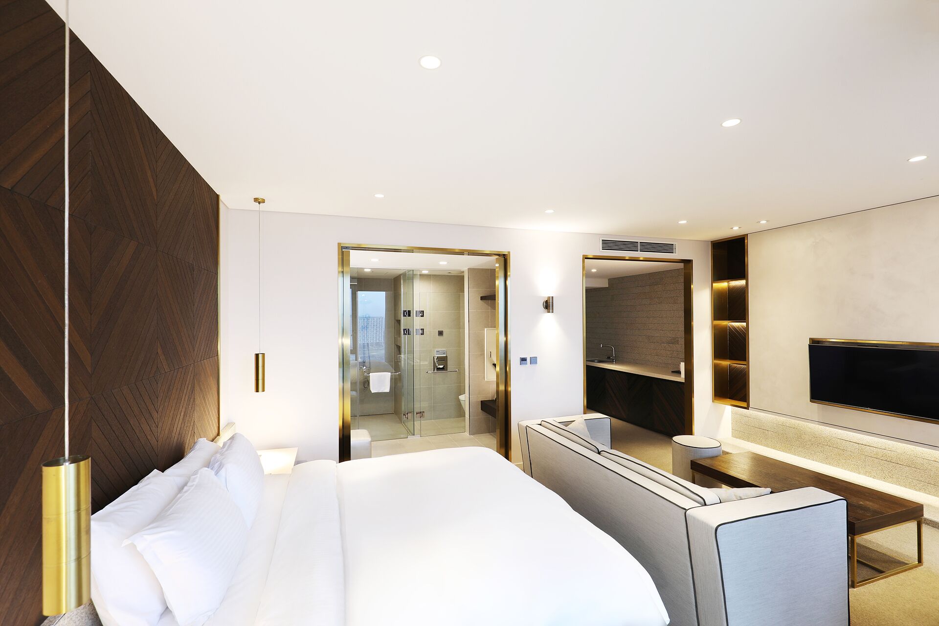 Quarto de hotel moderno com uma cama grande, uma escrivaninha com cadeira, televisão e área de chuveiro com divisória de vidro.