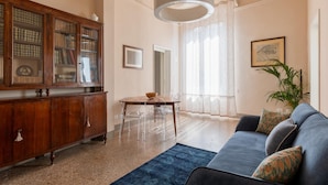 Uma sala de estar com um armário de madeira, uma mesa de jantar com cadeiras, um sofá azul e um lustre.