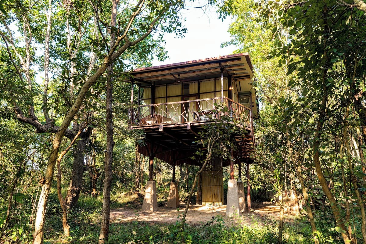 Uma casa na árvore com um deck de madeira e área coberta, cercada por uma floresta densa.