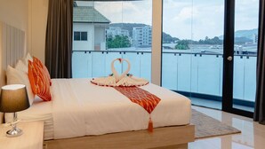 Quarto de hotel com uma cama grande, uma luminária de cabeceira e vista para edifícios pela janela.