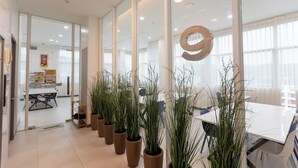 Um espaço de escritório moderno com paredes de vidro, um logotipo grande na parede e várias plantas em vasos.