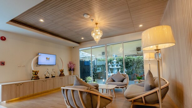 Um hall moderno com piso de madeira, um candelabro, uma TV fixada na parede e áreas de estar com almofadas.