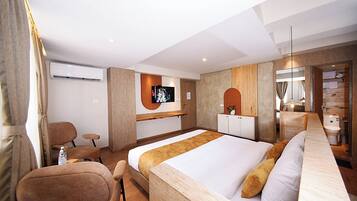 Quarto de hotel com cama, televisão, escrivaninha, cadeira e banheiro.