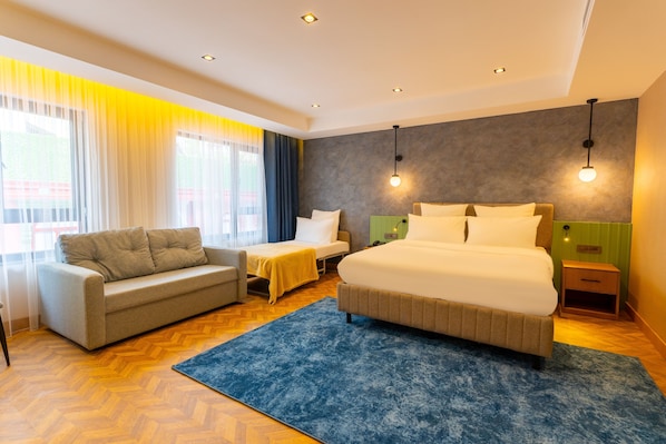 Quarto de hotel moderno com uma cama grande, um sofá, uma mesa pequena e uma mesinha de cabeceira.