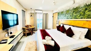 Quarto de hotel com cama, televisão, escrivaninha e um quadro na parede.