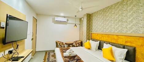 Quarto de hotel com cama, escrivaninha, televisão e ar condicionado.