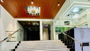 Uma escadaria moderna com degraus de mármore e guarda-corpos de vidro, que leva a um teto de madeira e um candelabro.