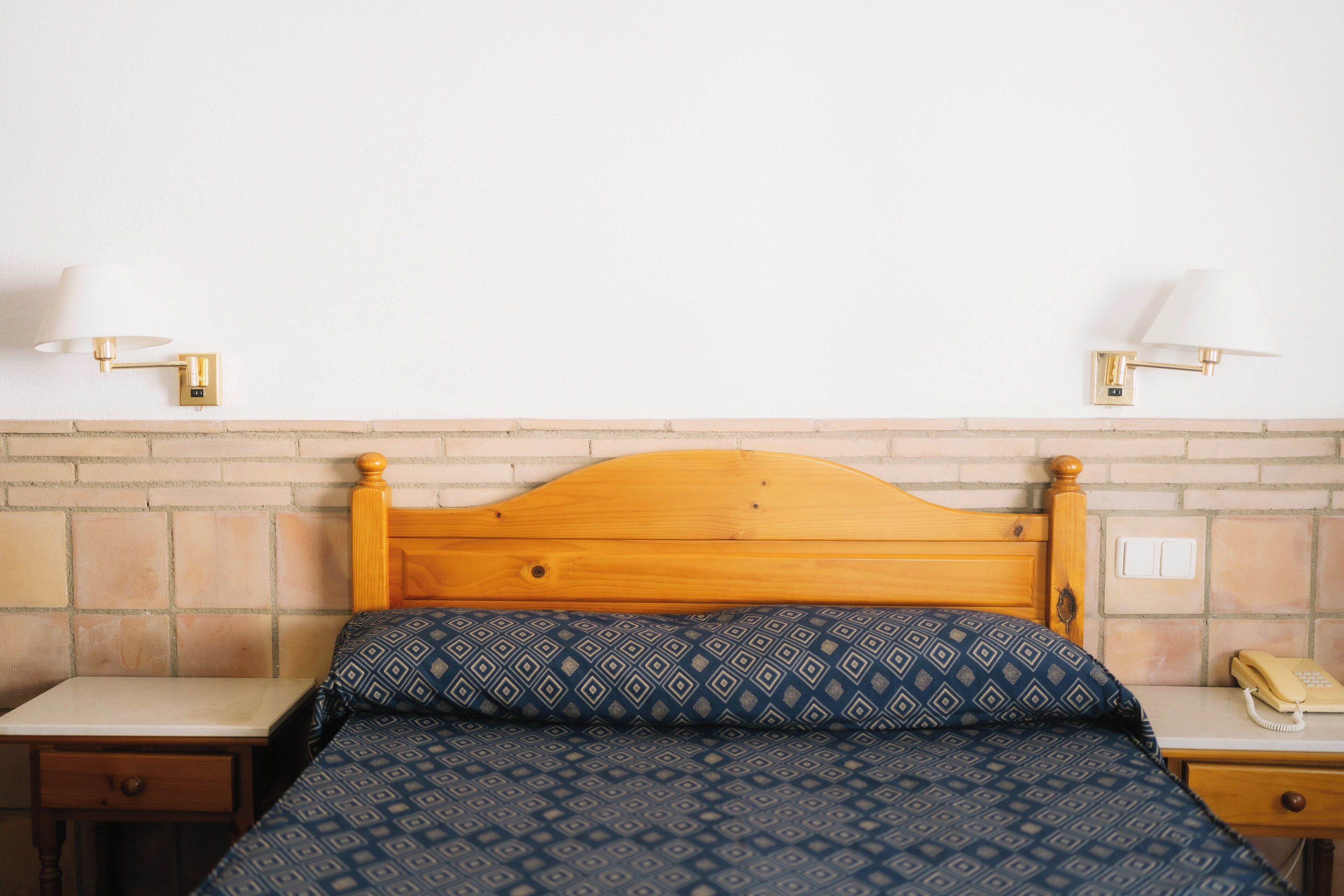 Quarto com cabeceira de madeira, colcha estampada, mesa de cabeceira com abajur e telefone.