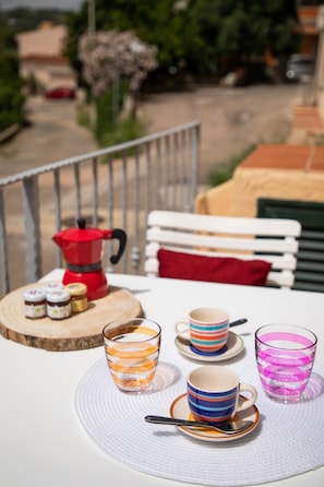 Uma mesa com uma cafeteira vermelha, potes de condimentos e copos e taças listrados sobre um jogo americano branco.