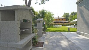 Um pátio com um banco de pedra, um pequeno jardim e um edifício com telhado de cerâmica ao fundo.