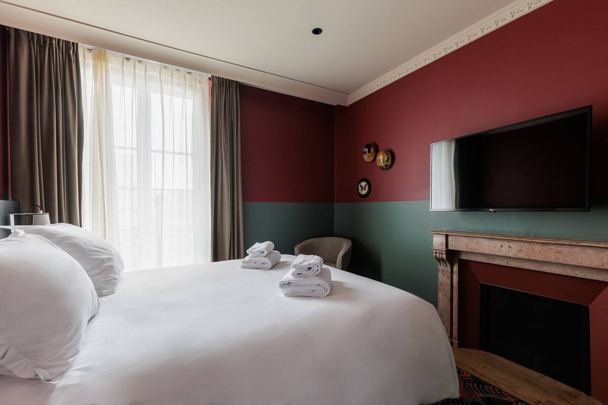 Quarto de hotel com uma cama grande, televisão de tela plana, lareira e janela com cortinas.