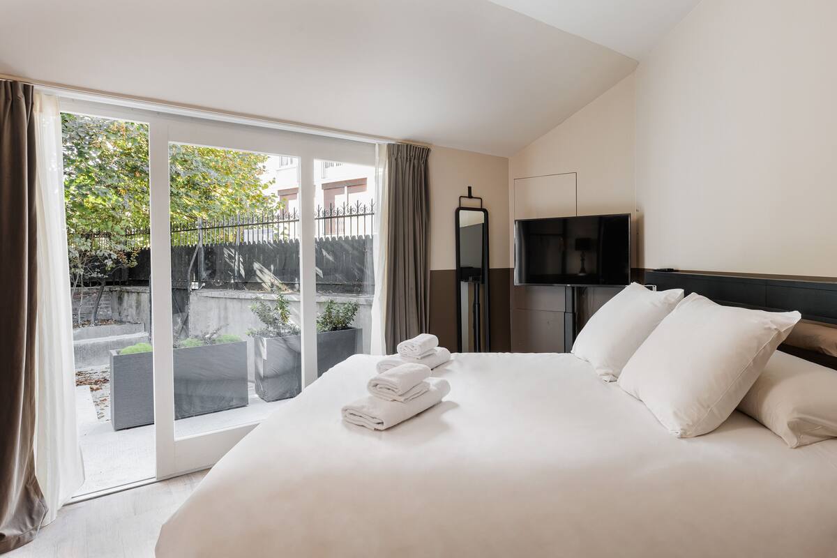 Quarto de hotel com cama grande, televisão e vista para um jardim através de uma porta de correr.