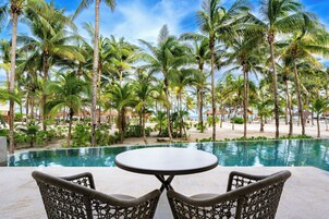 Área da piscina com duas cadeiras de vime e uma mesa, cercada por palmeiras e um céu azul límpido.