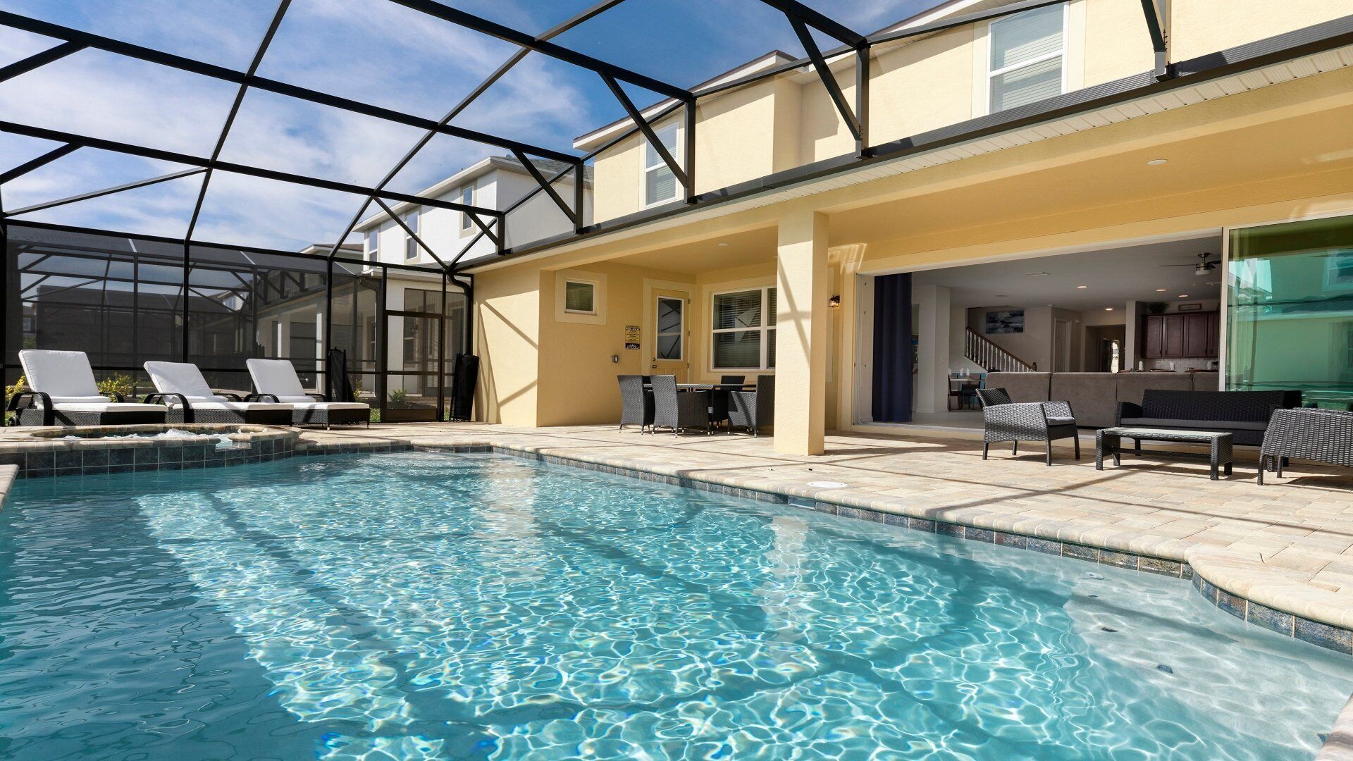 Piscina com espreguiçadeiras, área de varanda coberta e vista para o espaço de estar interno.