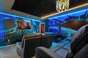 Sala de cinema em casa com tela grande, poltronas reclináveis e um painel decorativo na parede.