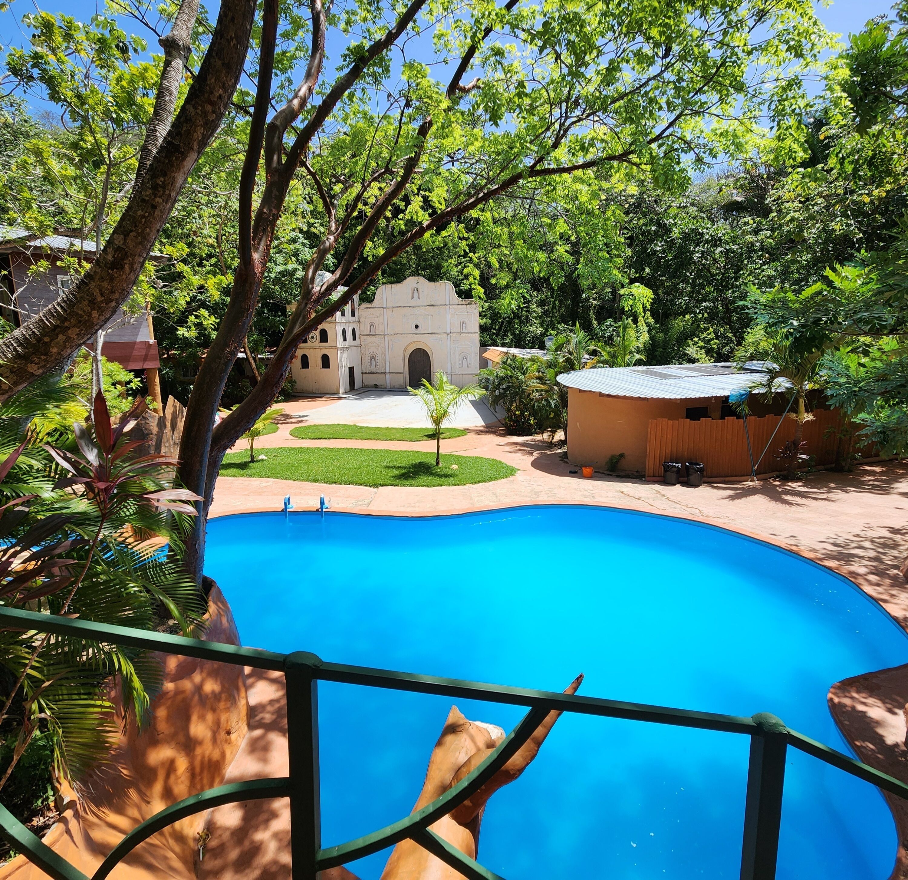 Piscina rodeada por vegetação exuberante e um edifício histórico.