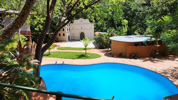 Piscina rodeada por vegetação exuberante e um edifício histórico.
