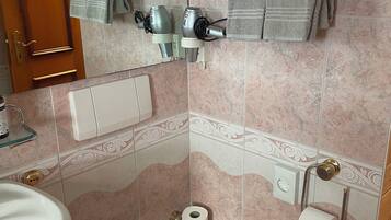 Casa de banho com sanita, lavatório, suporte de toalhas e aquecedor de toalhas.