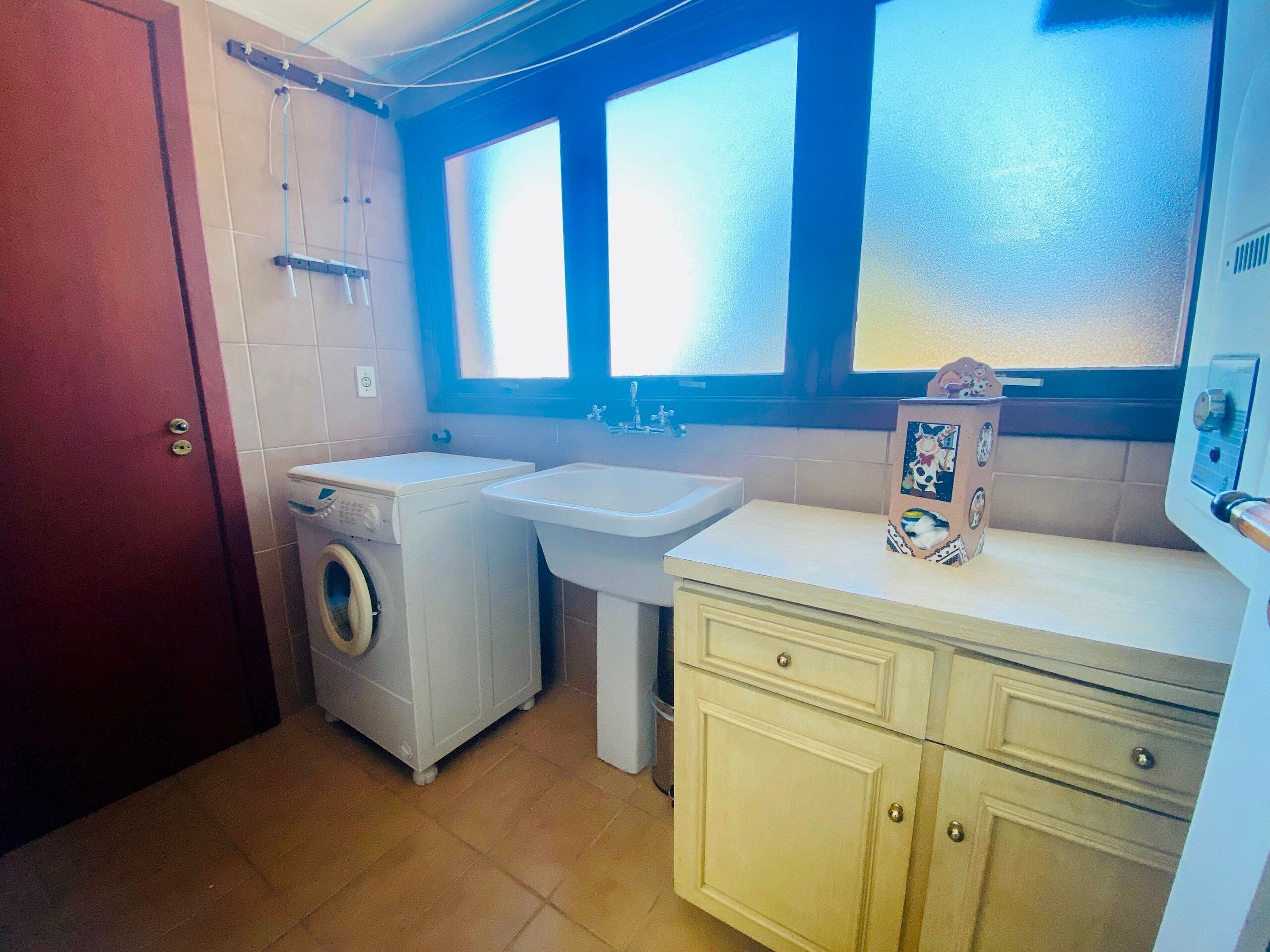 Casa de banho compacta com máquina de lavar roupa, duas pias e um armário com espelho.