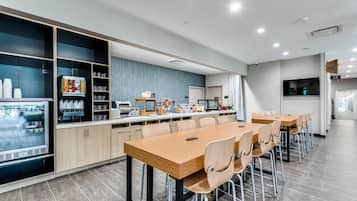 Um café moderno com um balcão comprido, área de estar e um refrigerador.
