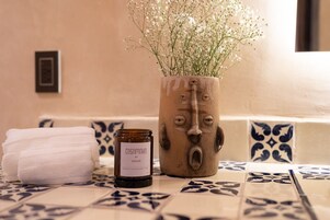 Casa de banho com um vaso de cerâmica com flores, uma vela e uma toalha num chão em mosaico.