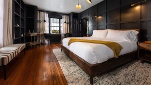 Quarto moderno com cama grande, painéis de madeira escura e uma escrivaninha com cadeira.