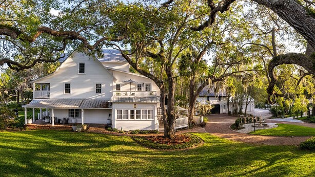 Uma casa branca com varanda, cercada por árvores e um gramado bem cuidado.