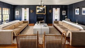 Sala de estar com paredes azul-escuro, lareira, dois sofás bege, uma mesa de centro branca e um candelabro.