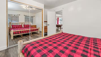 Quarto com um espelho grande, cama com colcha xadrez vermelha e preta, cabeceira de madeira e chão de madeira.