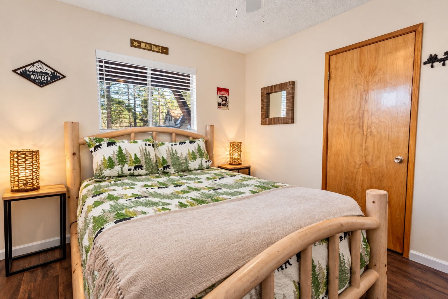 Quarto com cama, janela com persianas, porta de madeira e decoração de parede incluindo um aviso sobre trilhas para caminhada.