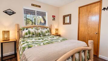 Quarto com cama, janela com persianas, porta de madeira e decoração de parede incluindo um aviso sobre trilhas para caminhada.
