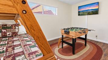 Quarto aconchegante com cama, mesa de pebolim, um quadro e uma janela.