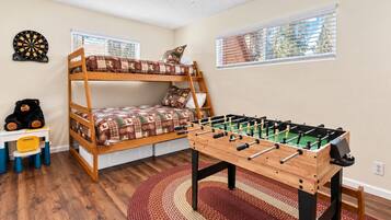 Uma cama de beliche com um alvo de dardos e uma mesa de futebol de mesa em um quarto com piso de madeira e um tapete vermelho estampado.