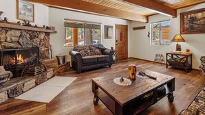 Uma sala de estar acolhedora com lareira de pedra, um sofá de couro e uma mesa de centro de madeira.