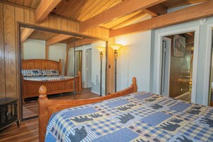 Um quarto com cama de madeira, colcha, espelho e corredor que dá para outro cômodo.
