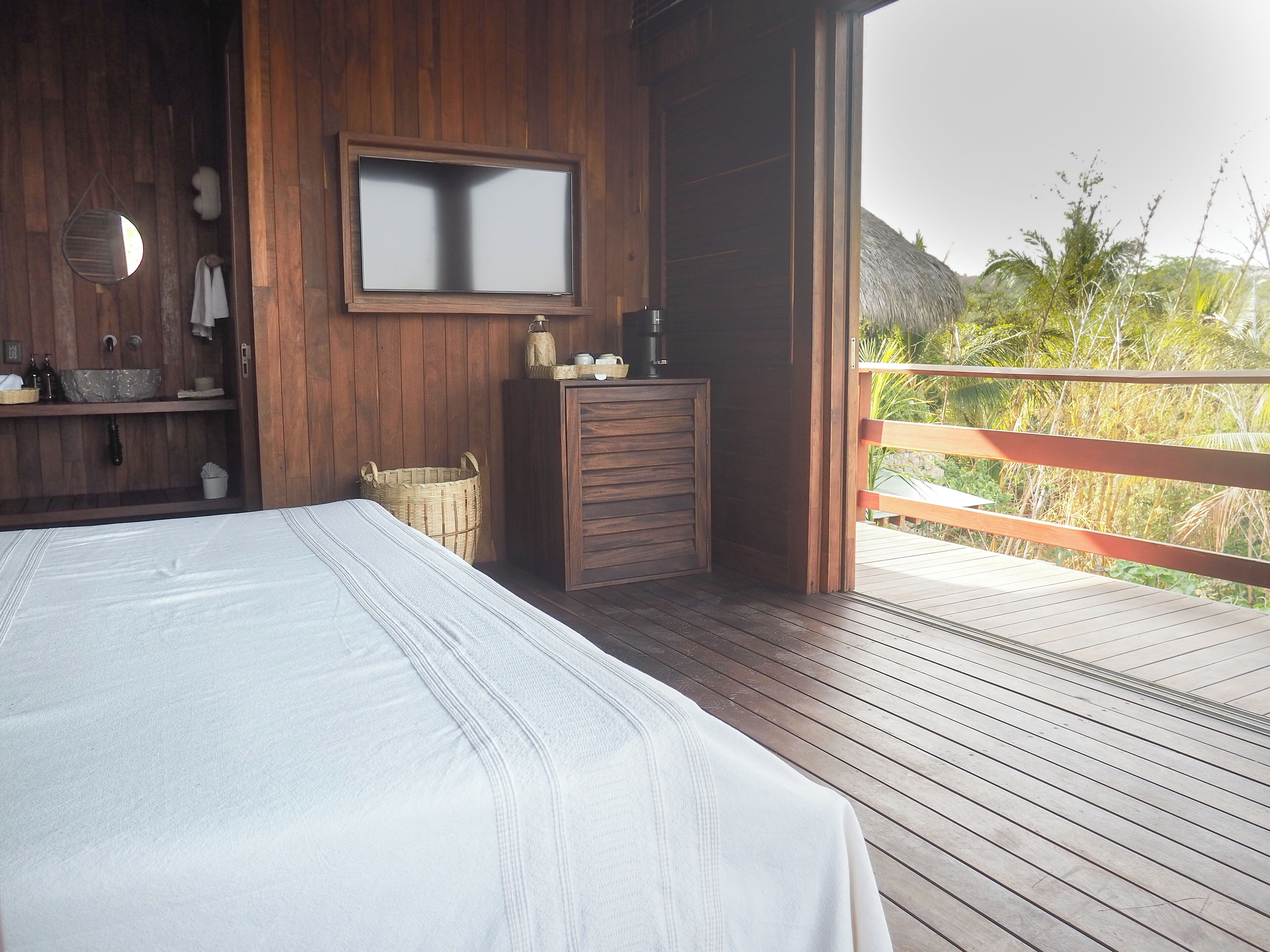 Quarto de madeira com cama, espelho, cômoda de madeira e vista para o exterior.