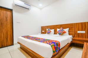 Uma cama bem arrumada com um edredom colorido estampado com padrão geométrico, uma cabeceira de madeira e uma mesinha de cabeceira de madeira com uma luminária.