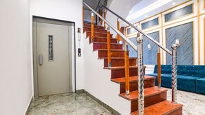 Uma escadaria com degraus de madeira e corrimãos de metal, um sofá azul e um chão de mármore.