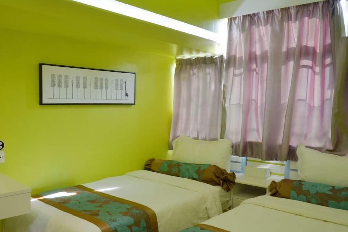 Quarto de hotel com duas camas, janela com cortinas leves, um quadro na parede e mesa de cabeceira com abajur.